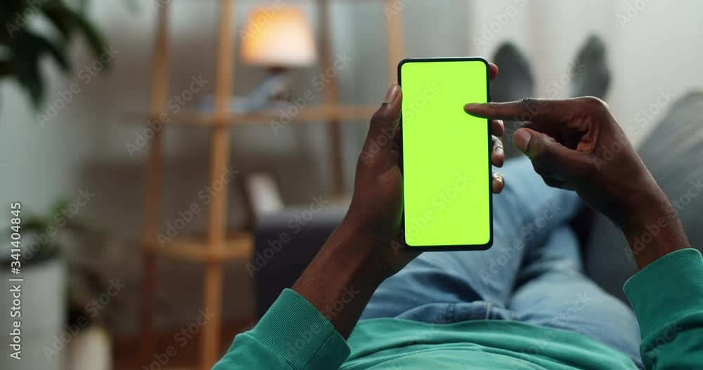 African american man scrolling mobile phone mock up screen while reading e book. Young man ...