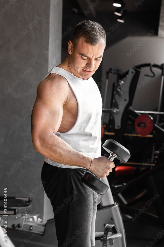 Bodybuilder doing biceps exersices with dumbbell in gym around fitness ...