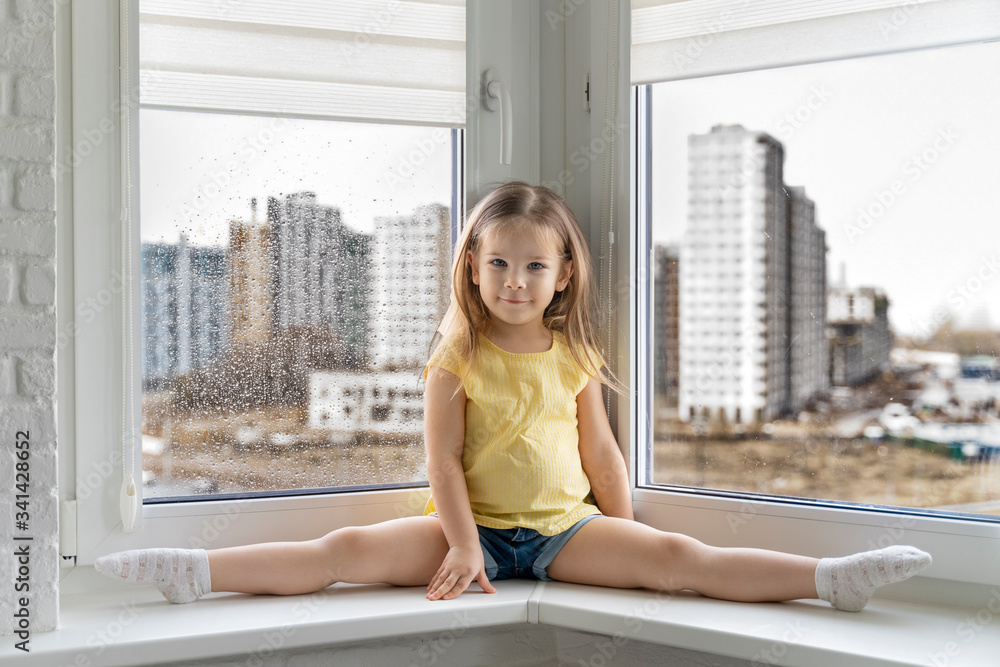 beautiful little girl sitting on the windowsill and smiling, looking at ...