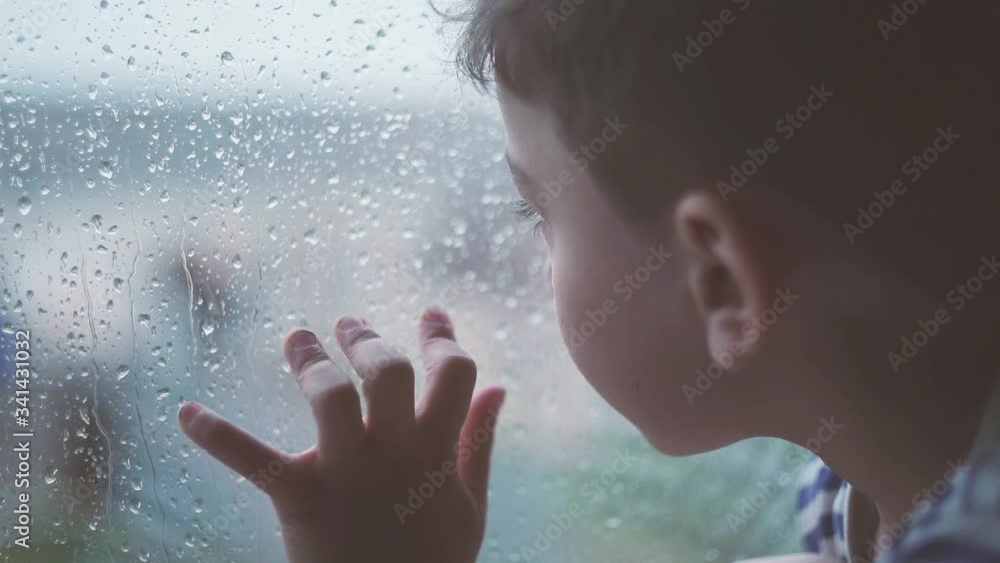 a little boy sits outside a rainy window and is sad. A window in rainy ...