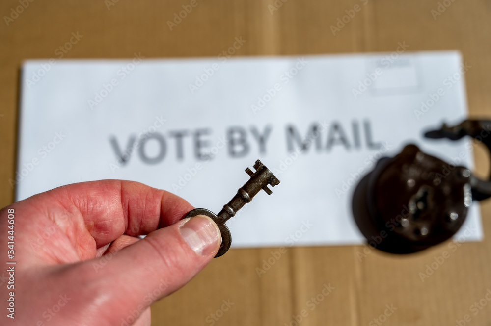 Hand holding a key in front of envelope for vote by mail ballot ...
