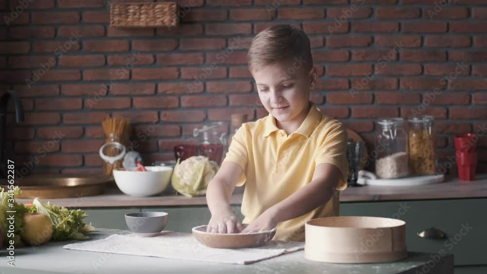 European young boy is cooking by himself in a modern kitchen. The kid ...