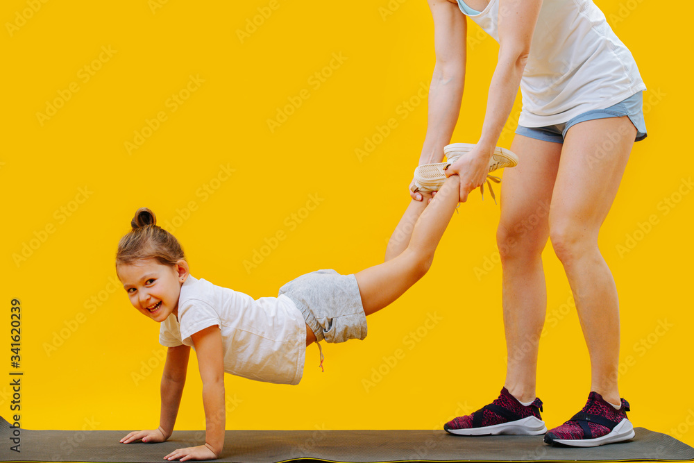 Little girl walking on hands with support from her mom over yellow ...