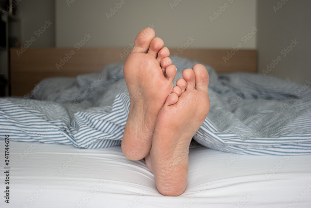 Caucasian male crossed feet sole sticking out from the quilt in bed ...