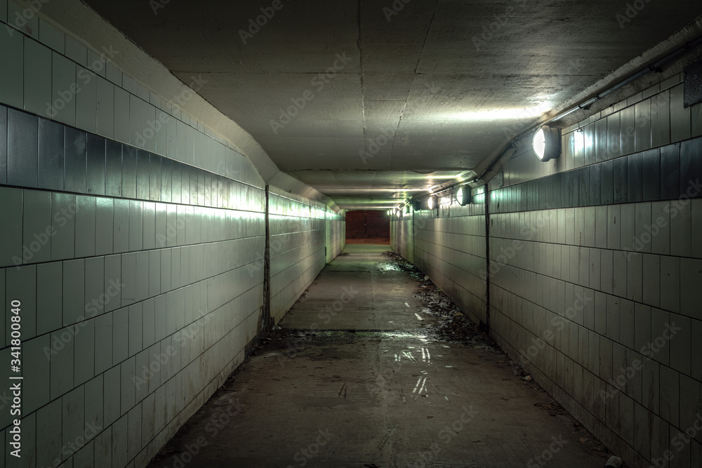 A view down a damp and dirty glazed tiled block and concrete tunnel ...