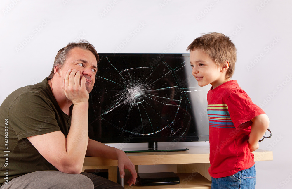 Little boy standing in front of a TV with broken screen and hiding a ...