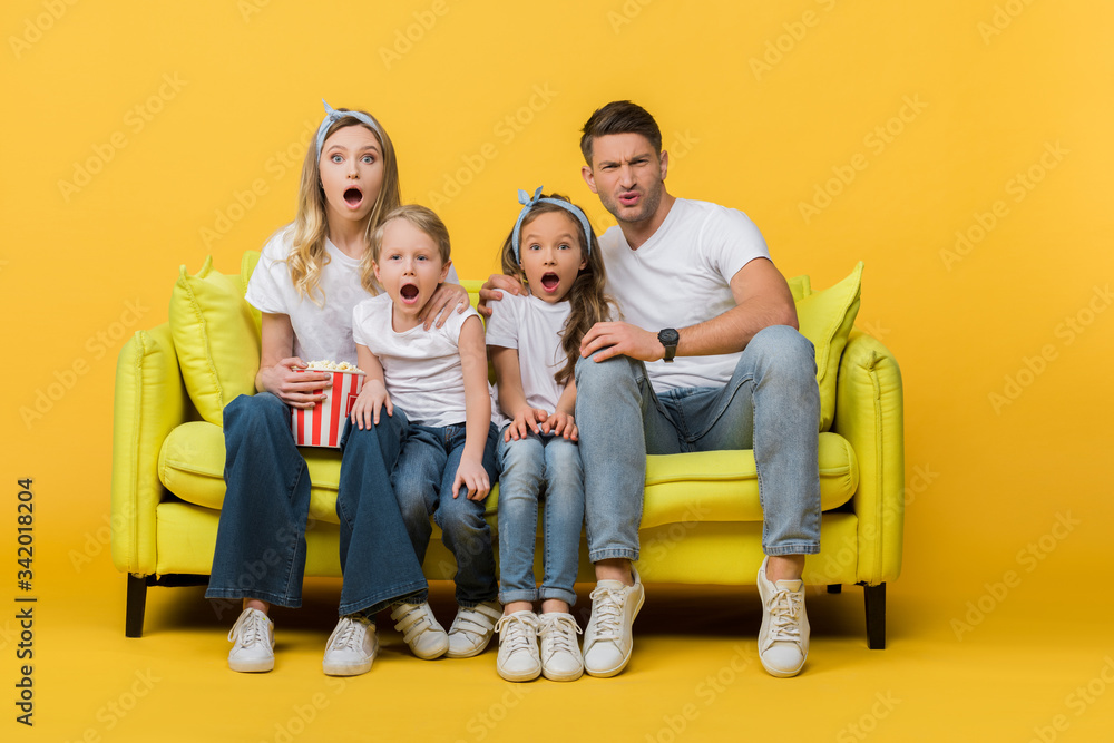 shocked family watching movie on sofa with popcorn bucket on yellow ...