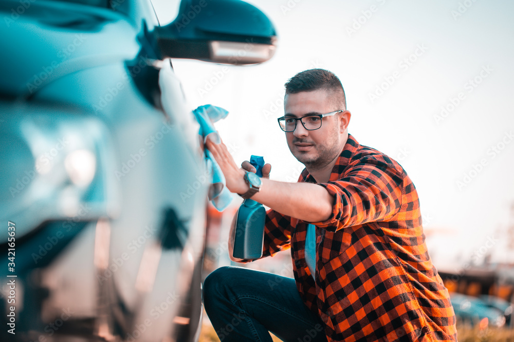 Young man polishing his car with a cloth and spray in a bottle ...