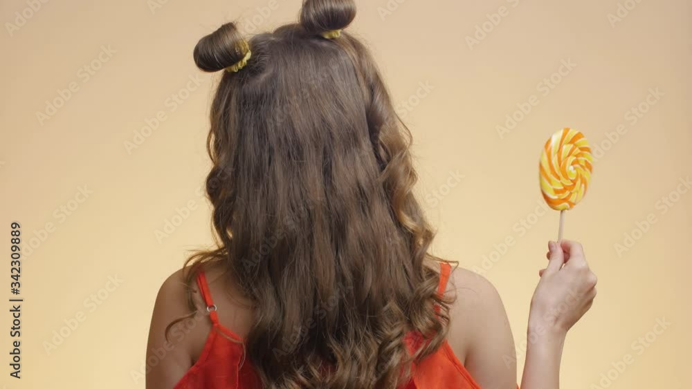 back of cute girl with big caramel candy on colored studio background ...