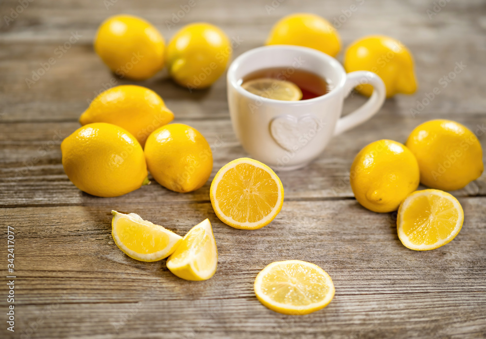 Cup of black tea with lemon slice and plenty of lemons around on grey ...