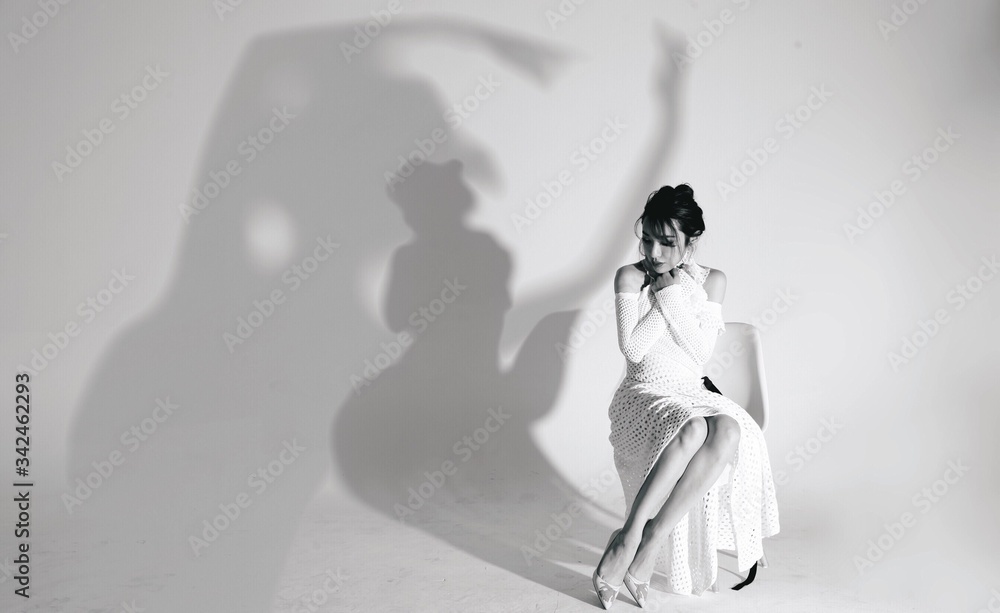 Full Length Of Fashion Model Sitting On Chair Against Shadow On White ...