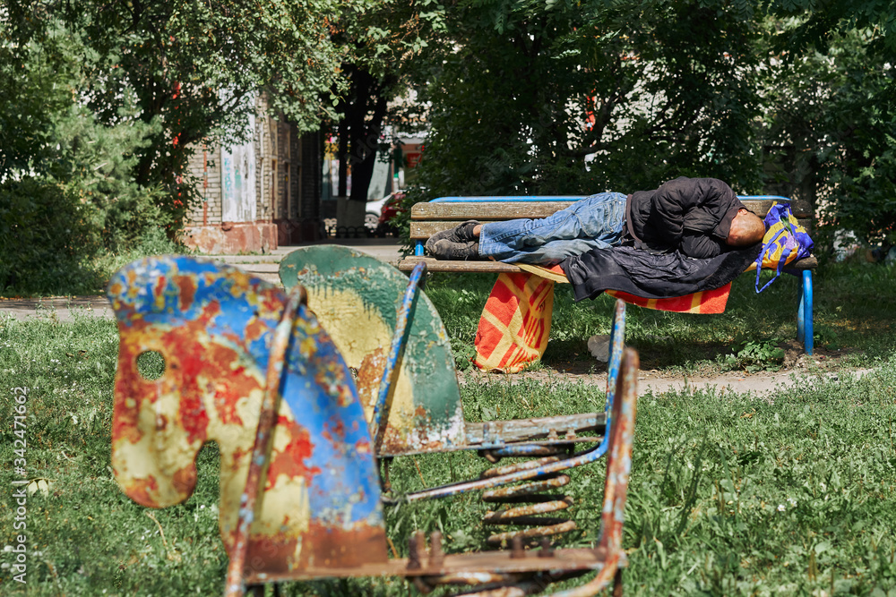 Homeless beggar man sleeping on a bench on the kids playground. Stock ...