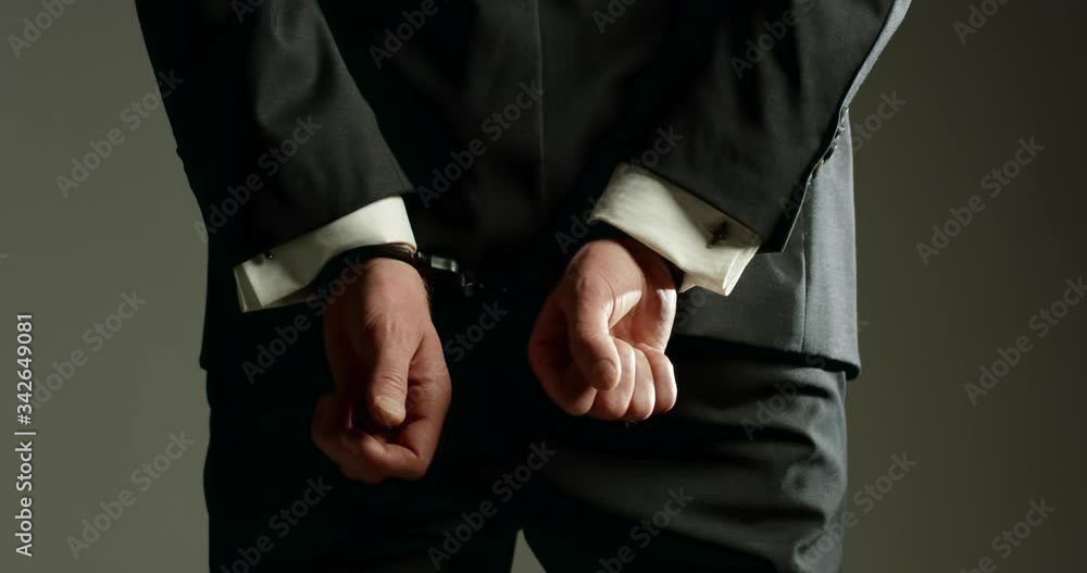 Business man in handcuffs behind back - close up on hands behind back ...