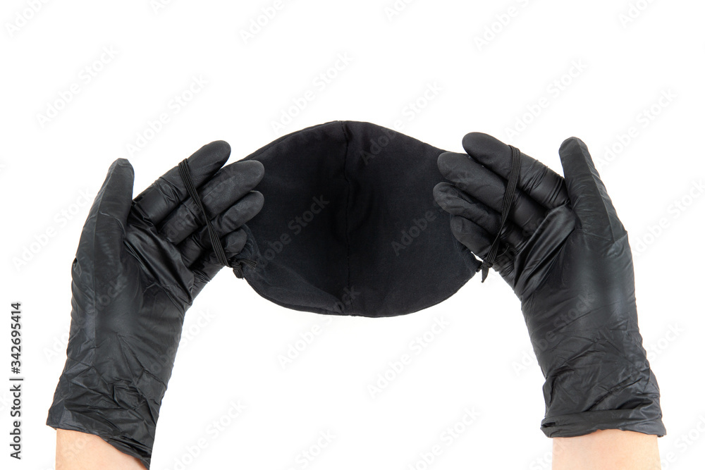 Female hands in black disposable gloves hold a black reusable face mask ...