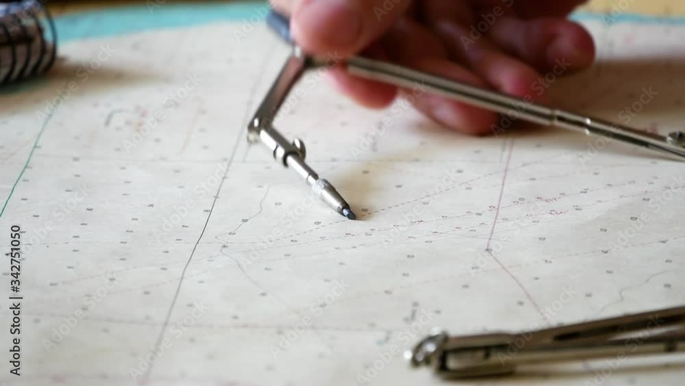 Close up of a man that draws an arc on the sea map with a compass, then ...