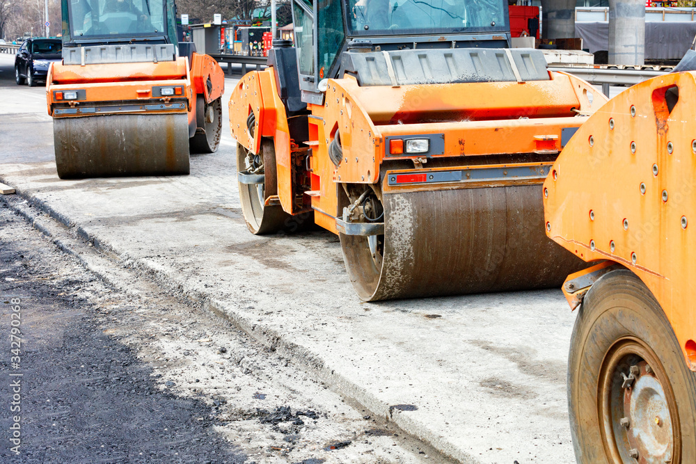Large and heavy orange vibratory rollers stand on the roadway awaiting ...