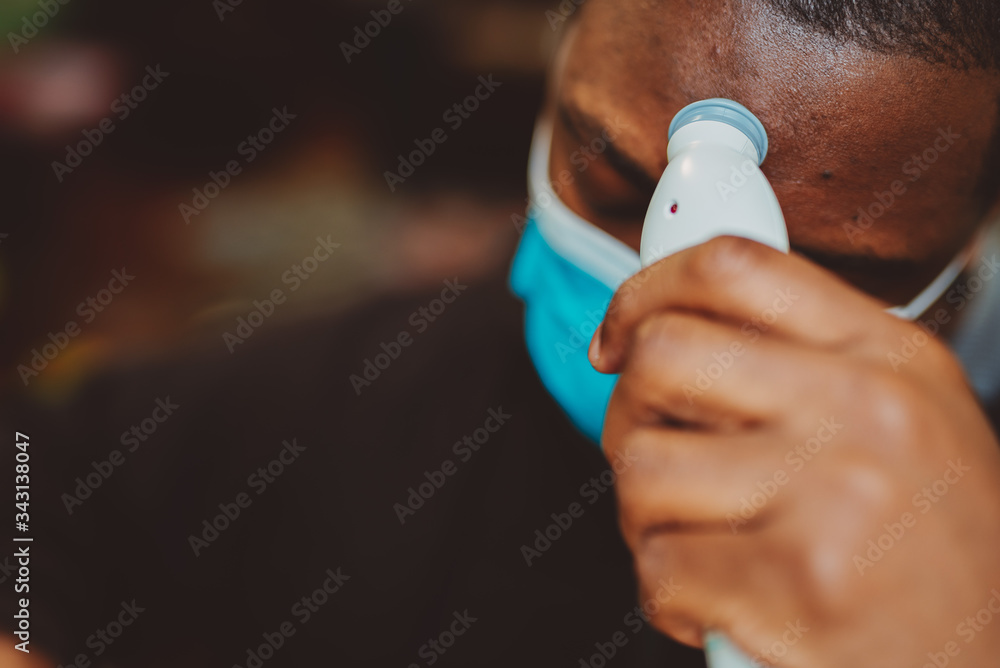 African american man using a temporal thermometer to record his ...