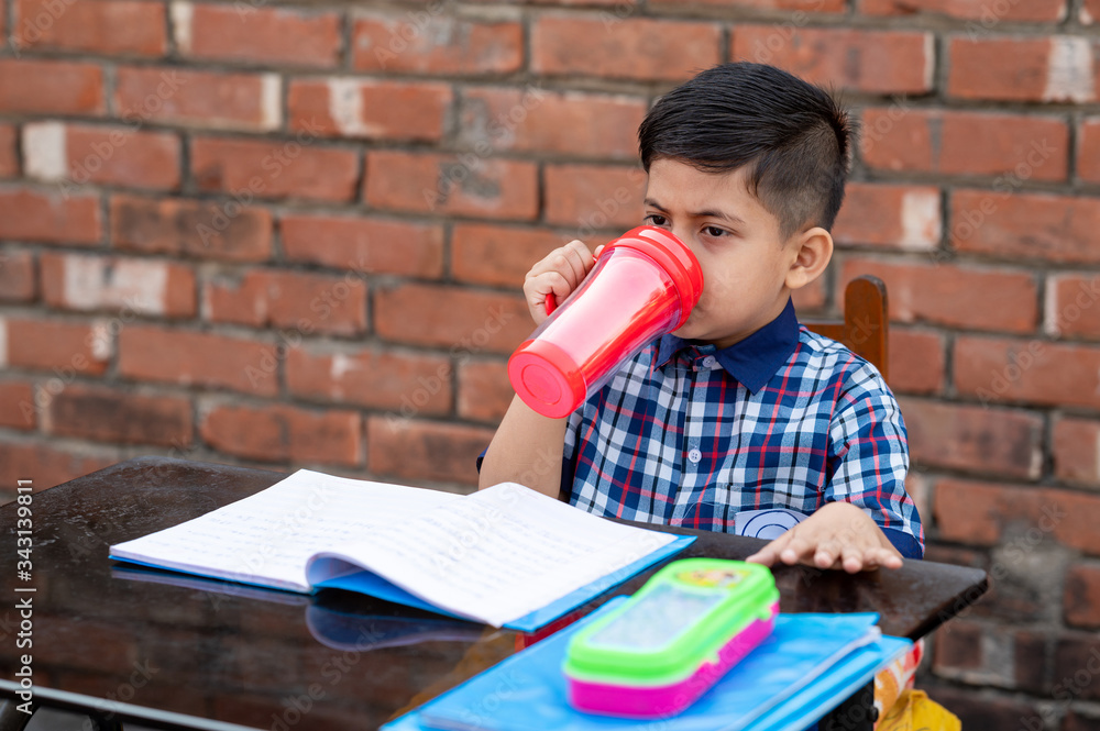Primary school student drinking water with red water bottle while ...