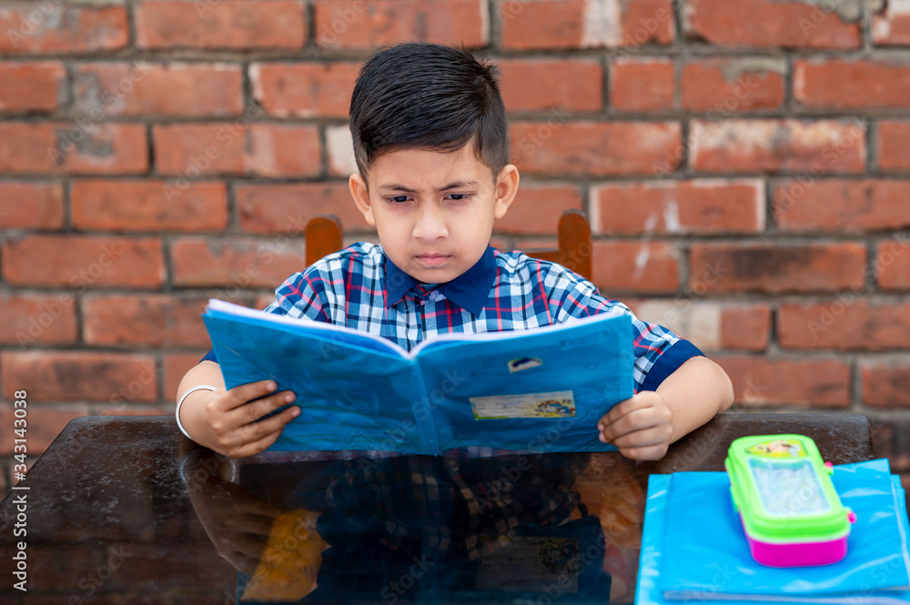 Primary school student in proper school uniform reading book on study ...