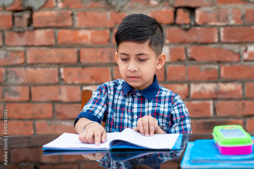 Primary school student in proper school uniform reading book on study ...