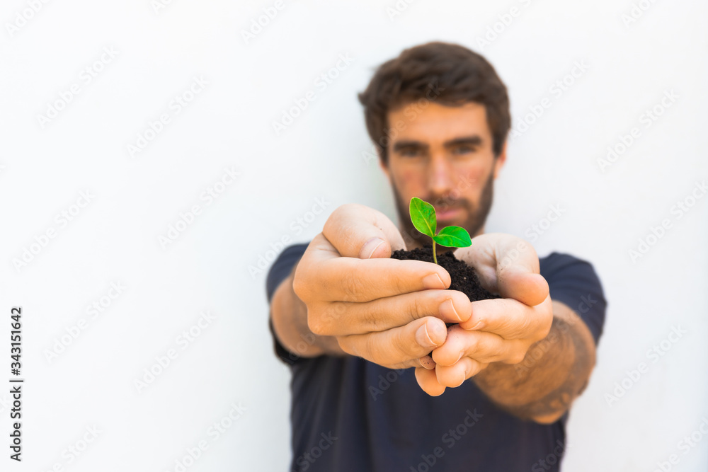 Man holding a little growing plant in front of his blurry face. Eco ...