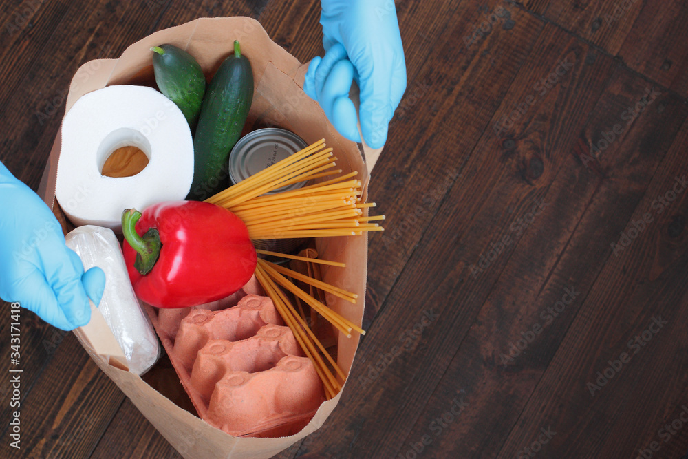 Person in blue gloves opens a paper bag with a set of products: pasta ...