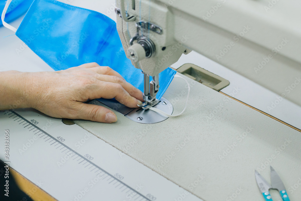 Stepwise stitching of blue fabric medical masks on a sewing machine. A ...