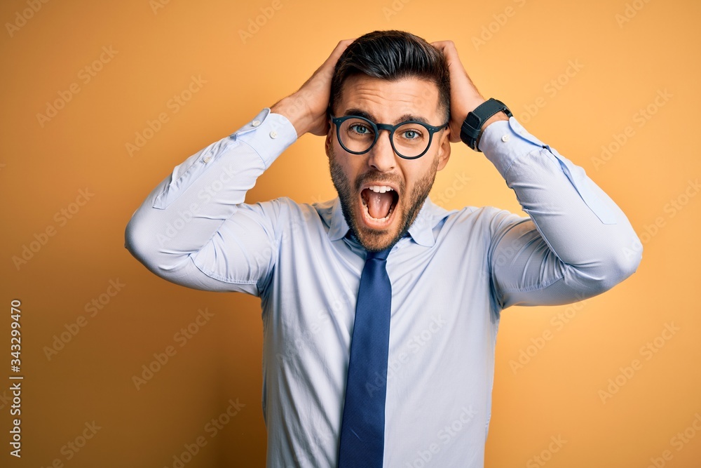 Young handsome businessman wearing tie and glasses standing over yellow ...