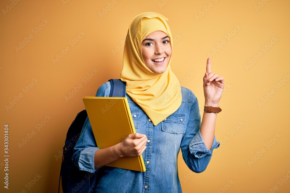 Young student girl wearing muslim hijab and backpack holding book over ...