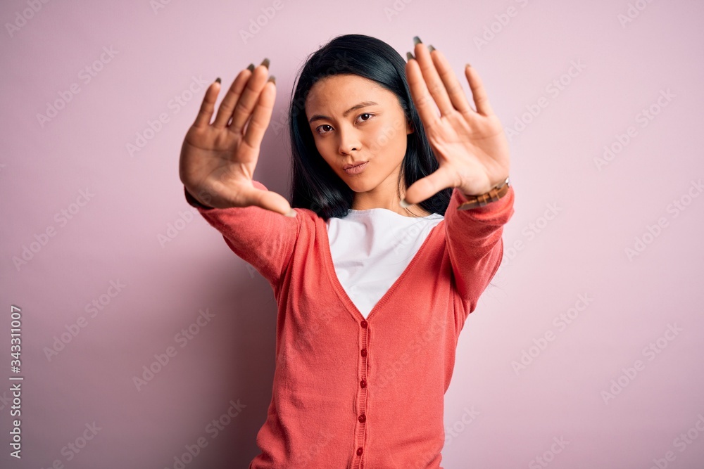 Young beautiful chinese woman wearing casual sweater over isolated pink ...