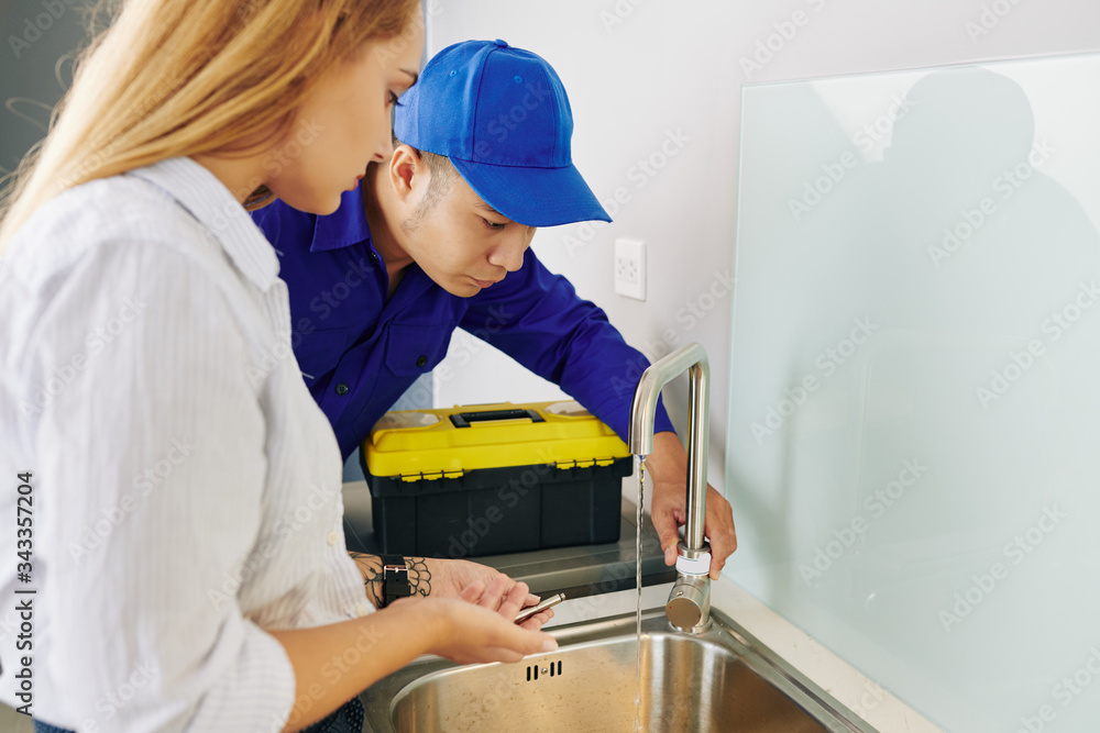 Female customer showing repairman her broken water tap in kitchen sink ...