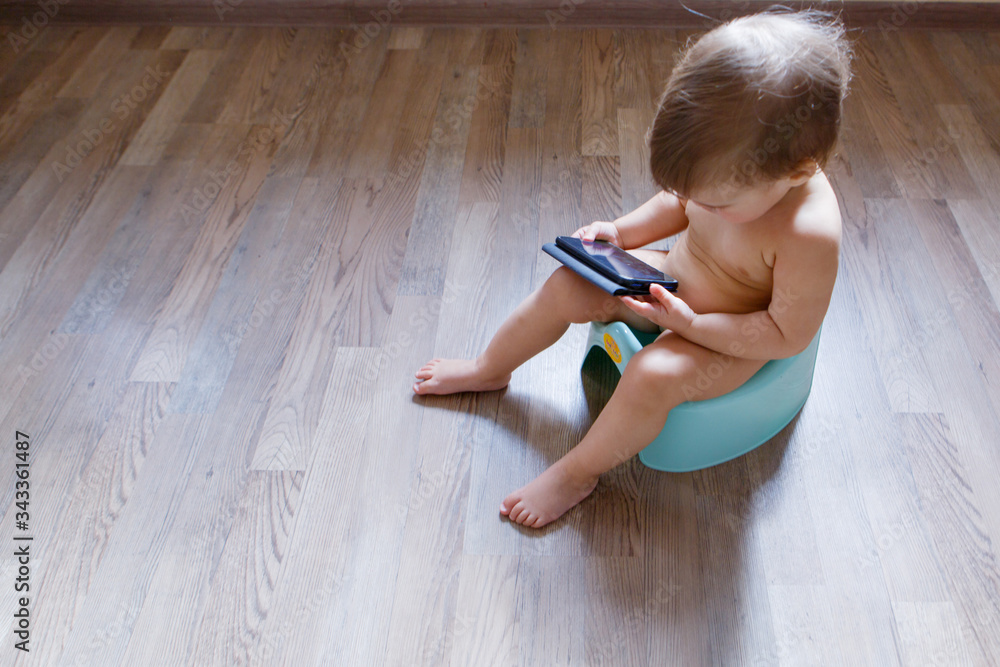 little girl is sitting on potty and playing with her phone. viewing ...
