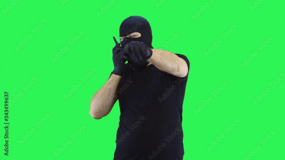 A man in a balaclava talking on a walkie-talkie makes a choice with his ...