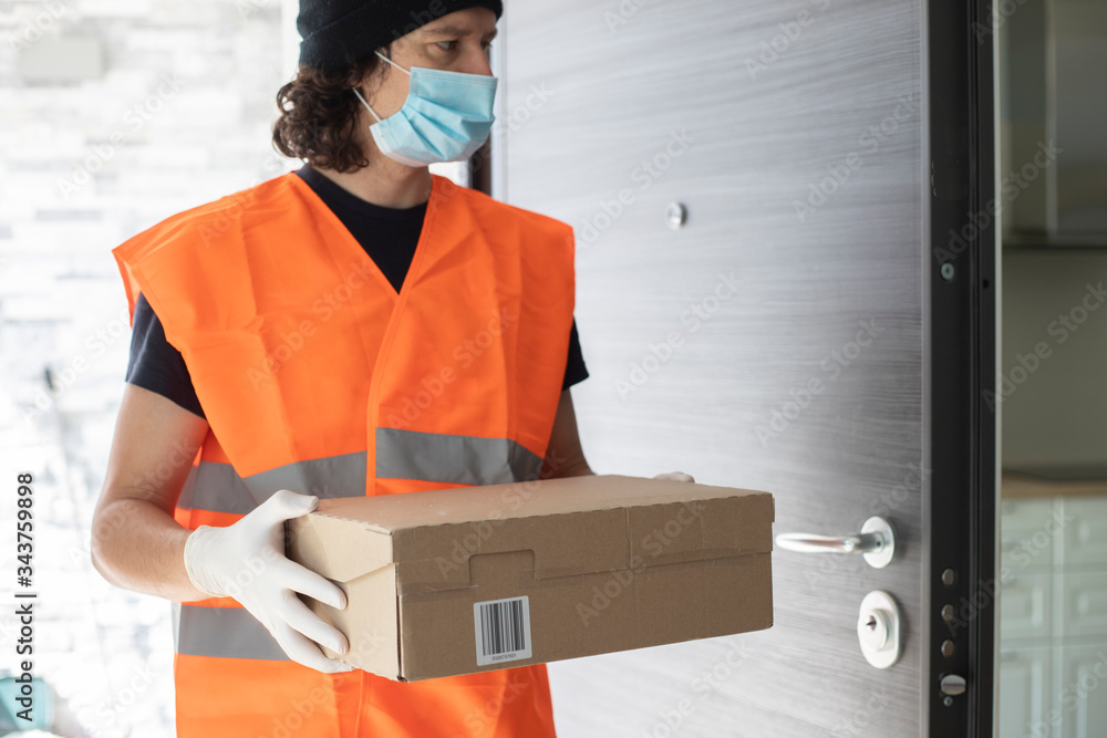 Young delivery man at front door with a parcel box, wearing gloves and ...
