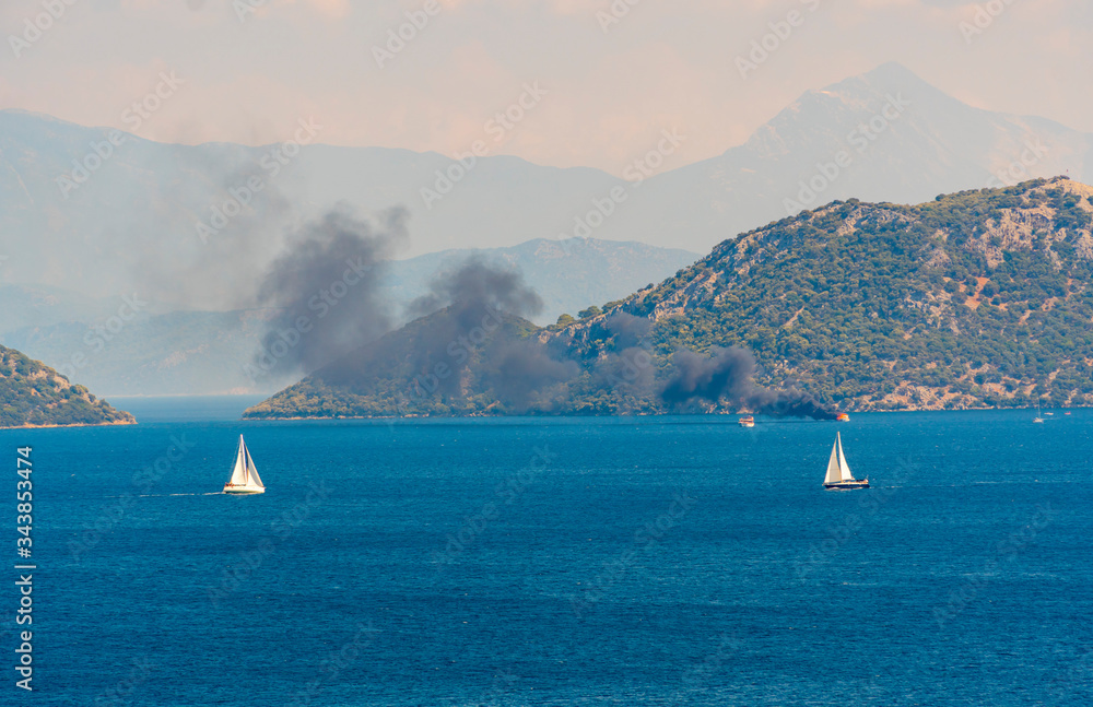 Dark smoke covering the air of a boat on fire at sea. Blue waters with ...