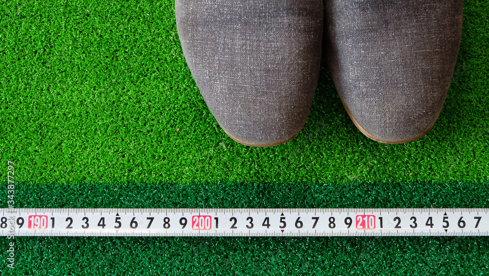 The tip of a pair of gray shoes with a measuring tape in front, showing ...