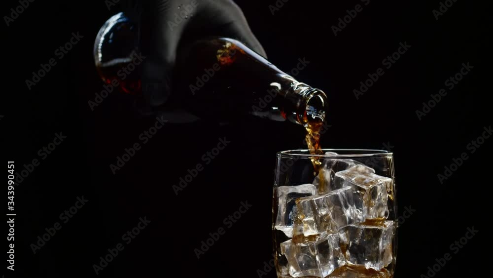 Pouring cola, pepsi with ice cubes close-up. the bartender's hand pours from a bottle of cola ...