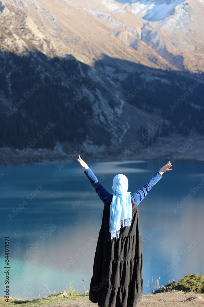 Muslim girl stands with her back and raised her hands up. Almaty peak ...