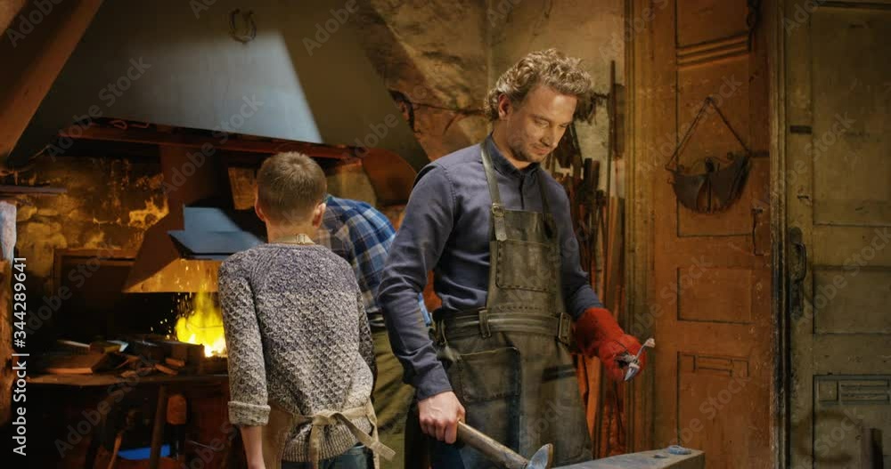 Caucasian teen boy coming in smithy where his father and grandfather ...