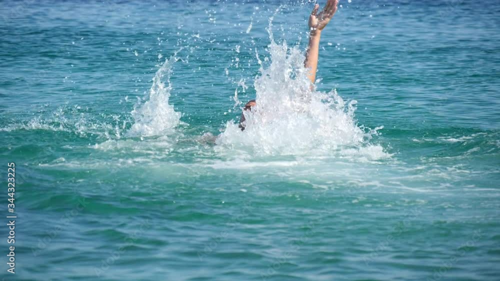A young bald man swims on his back in blue, turquoise sea, rakes water ...