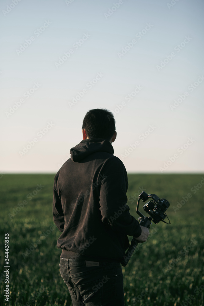 young male video operator standing in the green field with ...