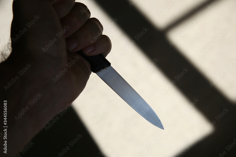 A hand holding a knife in shadow. This image can be used to represent ...