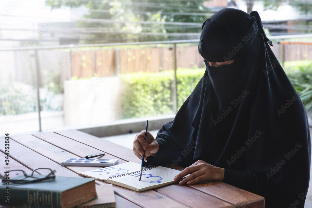Women wearing niqab practice writing Arabic handwriting with ink ...