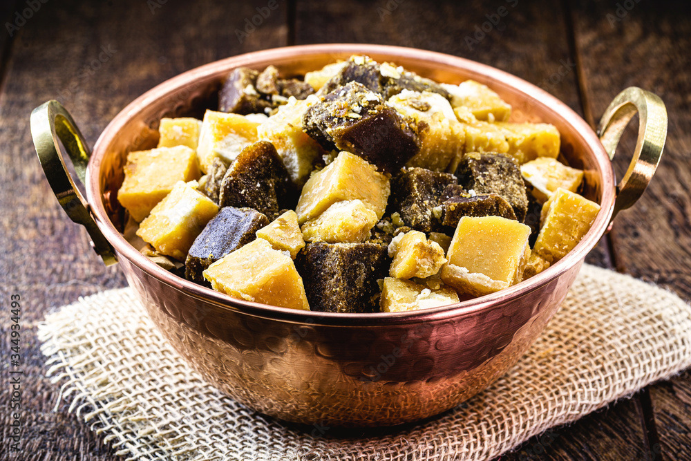 Candy in a copper pot on a rustic table. Rapadura is a sugar cane-based ...