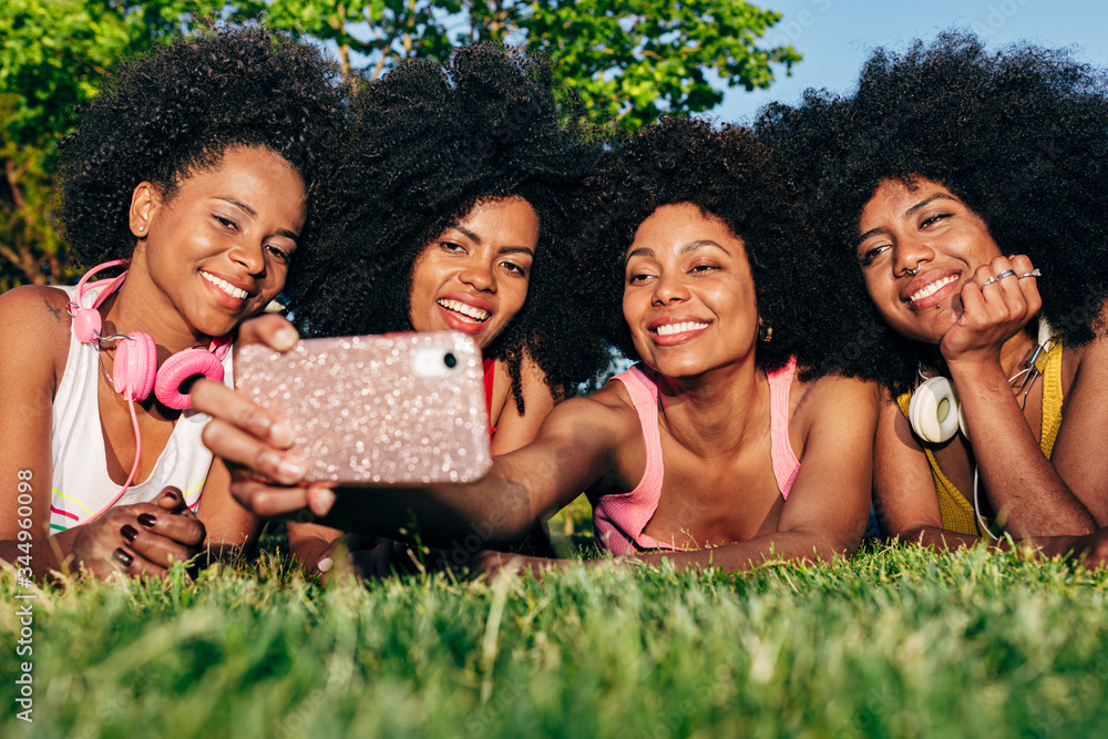 Stockfoto Afro women friends hanging out in the park using a cellphone ...