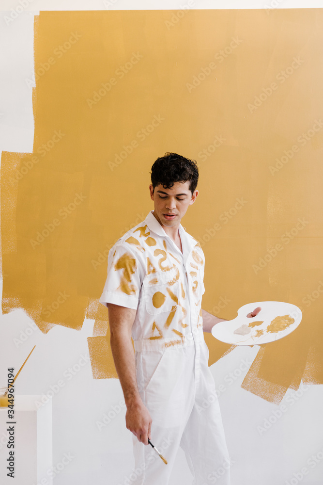 young man with paint palette painting a gold background in white ...