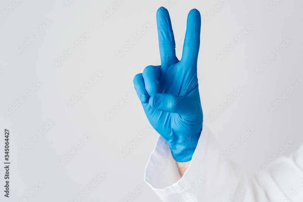 V sign is showed by hand in a blue medical glove on a white background ...