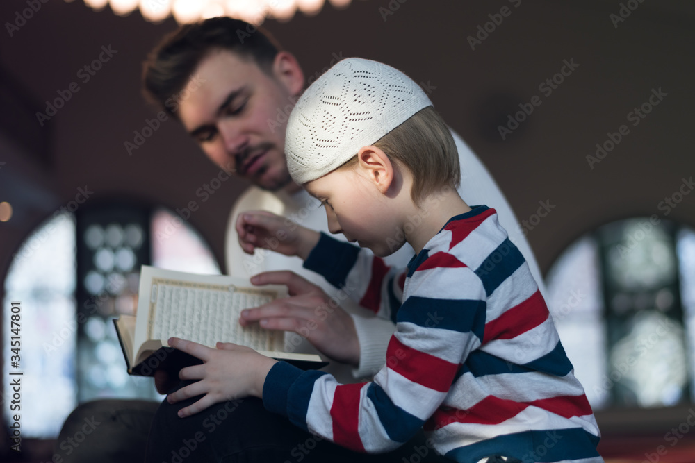 Religious Muslim Man teaching his little son to pray to God with Koran ...