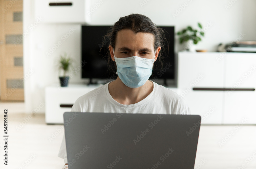 Man in medical mask is working from home with a laptop because of ...