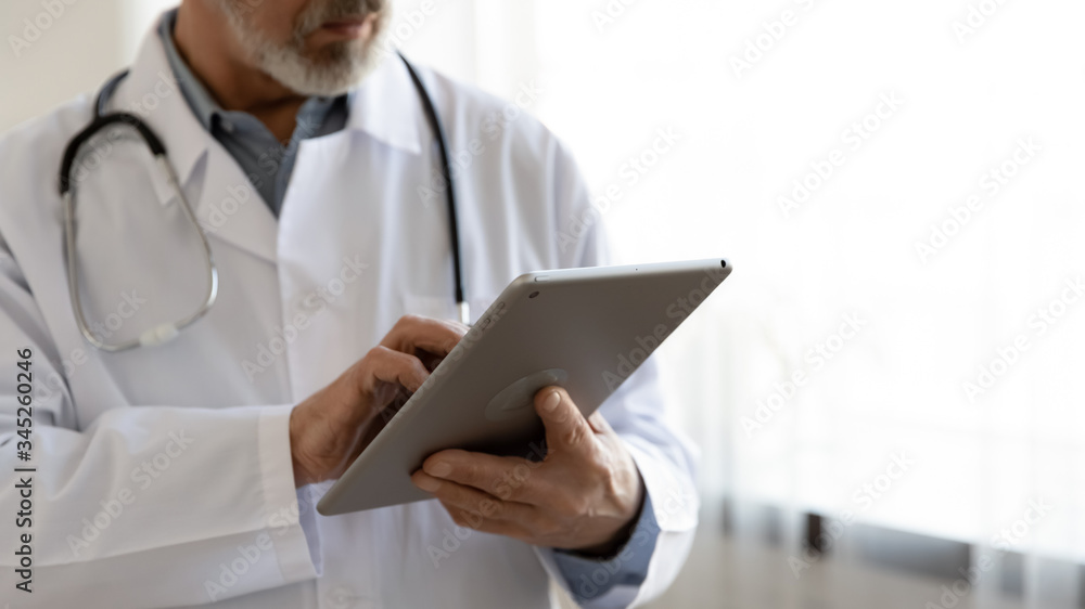 Old male doctor holding modern digital tablet computer standing in ...